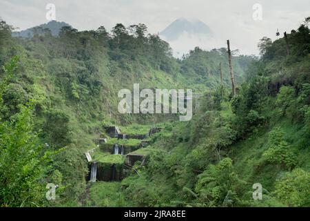 A waterfall and mount Merapi volcano as seen from Plunyon Kalikuning in ...