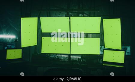 Modern computers with green screens placed on desk in dark room with ...