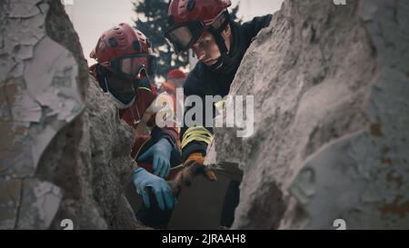 Black rescuer talking with colleague while sitting near rubble and ...