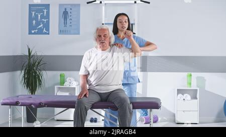 Female doctor stretching arm of relieved senior male patient during ...