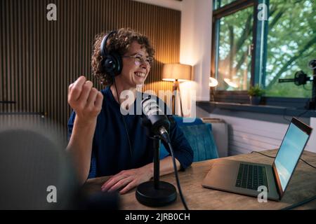 Presenter wearing headset recording through microphone at radio station ...