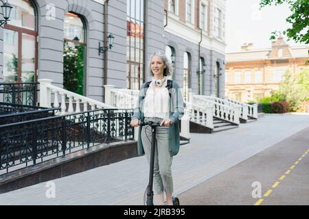 Smiling woman riding electric push scooter on road Stock Photo - Alamy