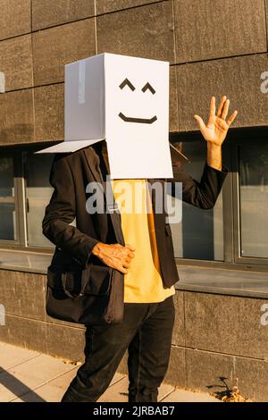 Businessman gesturing with a cardboard box on his head with smiley face ...