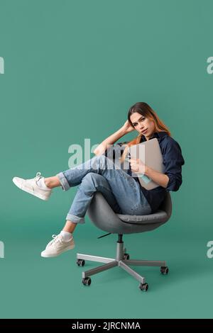 Transgender programmer with laptop sitting on chair against green ...