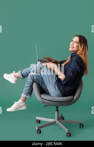 Transgender programmer with laptop sitting on chair against green ...