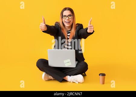 Transgender programmer with laptop showing thumb-up at table on pink ...