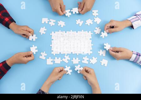 Businesspeople Solving White Jigsaw Puzzle Together On Wooden Desk ...