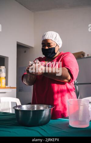 Venezuelan female in cloth face mask preparing arepas at table with ...