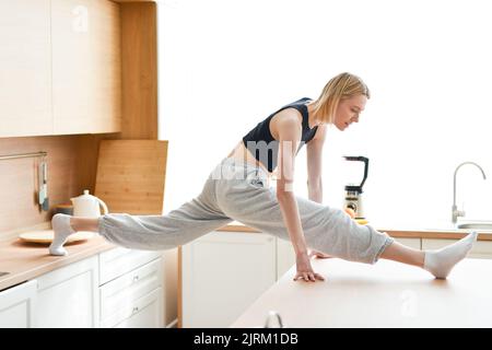 Woman doing the splits in kitchen between tables Stock Photo - Alamy