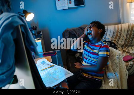 Black boy doing homework with computer while sitting at table in home ...