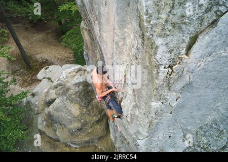 Determined climber clambering up steep wall of rocky mountain ...