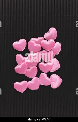Pink silk decorative hearts scattered on black textured paper. Copy ...