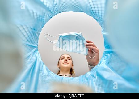 Woman throwing used medical mask into plastic container outdoors Stock ...