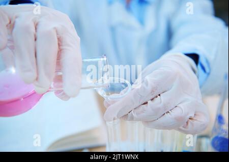 Scientist pouring pink substance from one flask to another in a ...