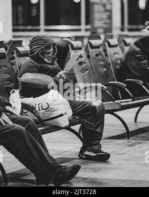 A grayscale shot of a homeless man sleeping in a metro station in Paris ...