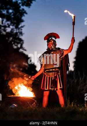 Roman living history reenactor holds a flaming torch next to a fire ...
