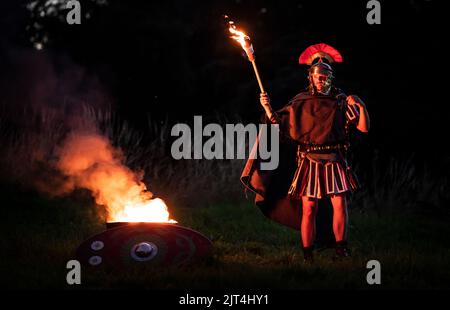 Roman living history reenactor holds a flaming torch next to a fire ...
