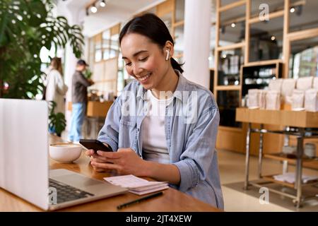 Young Asian woman smiling using laptop drinking beverage at home office ...