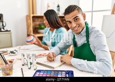 Young latin painter couple smiling happy sitting on the floor painting ...