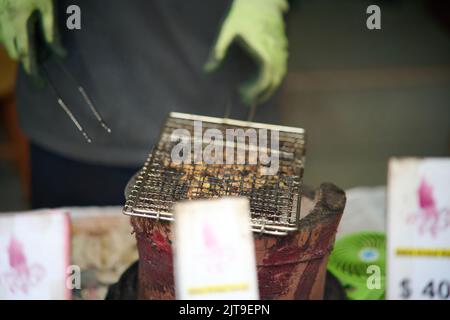 A closeup of a man cooking Tai Charcoal barbeque seafood on a stove ...