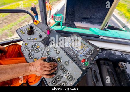 Worker, operator is controlling tarmac road laying machine with ...