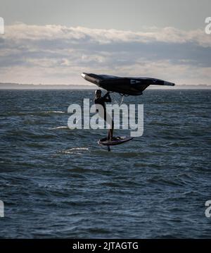 A wing foiler enjoying riding above the waves on a windy day in New ...