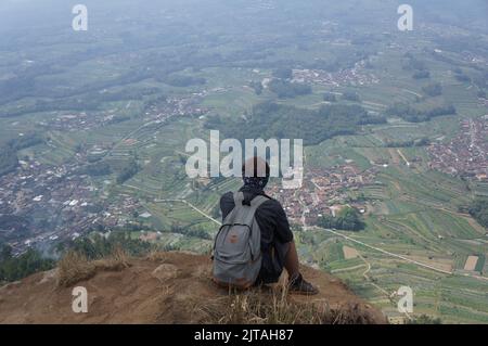 Magelang, Indonesia - A man sits at the edge of Andong mountain seeing beautiful green scenery ...