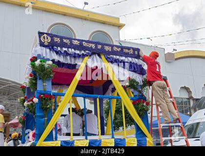 A Sikh man puts bunting on the mani float of the 2022 Nagar Kirtan ...