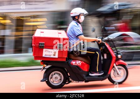 A Japanese postal worker delivers mail by electric delivery scooter ...