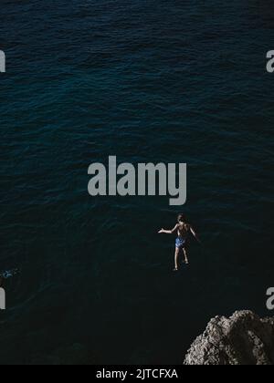 A view of a male jumping into the calm sea from a cliff Stock Photo - Alamy