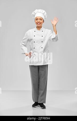 Beautiful young female chef waving hands on blue background Stock Photo ...