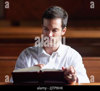 Young man with Holy Bible praying on white brick background Stock Photo ...