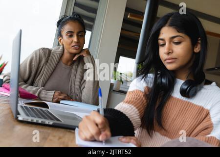 Biracial mother writing in book while teaching teenager daughter on ...