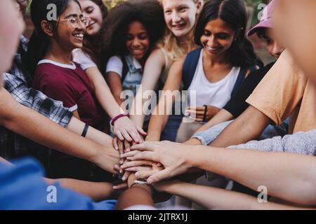 Multicultural teenagers smiling happily while putting their hands together in a huddle. Group of ...