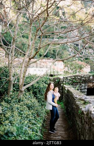 Kid stands near the stone fence of the house and looks at the cat ...
