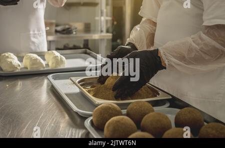 A farmer in black gloves sprinkle black pepper on a cheese ball. The ...