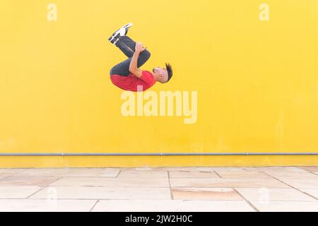 Male jumping near yellow wall and showing somersault while doing ...