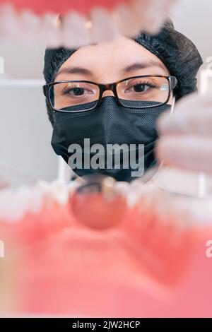 Young female dentist with dental mirror and tooth model on blue ...