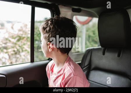Kid with lollipop sitting on back seat of car and looking out window ...