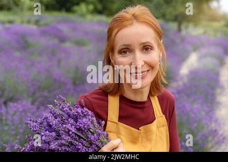 Calm mature female gardener with red hair in casual clothes and apron ...