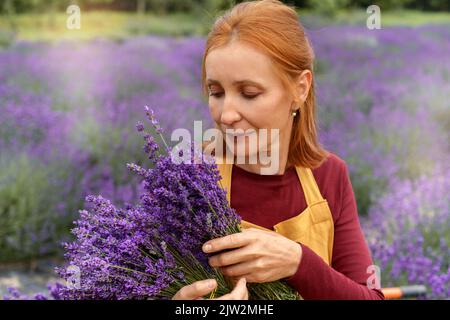 Calm mature female gardener with red hair in casual clothes and apron ...