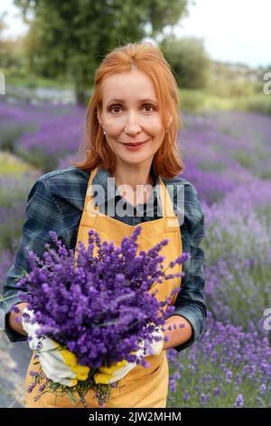 Calm mature female gardener with red hair in casual clothes and apron ...
