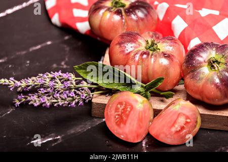 Tiger tomato on a cutting board with basil leaves on wooden background ...