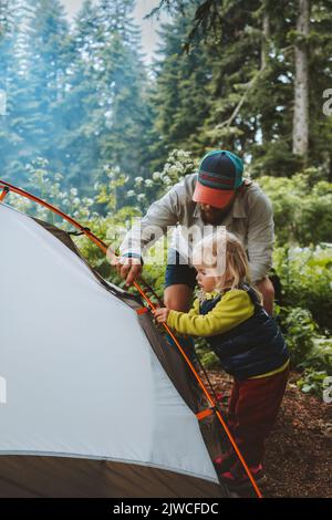 Family camping outdoor child helps to set tent father and daughter ...