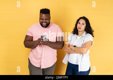 offended african american man using smartphone on orange background ...