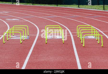 Three rows of yellow mini hurdles set up in lanes on a track for agility training during track ...