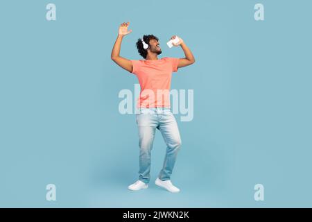 Cool eastern guy singing and dancing on blue, showing smartphone Stock ...