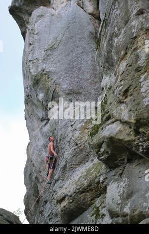 Determined climber clambering up steep wall of rocky mountain ...