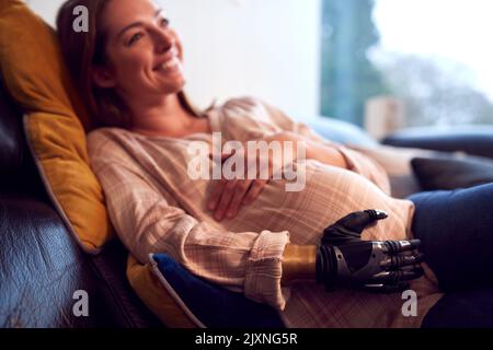 Close Up Of Pregnant Woman With Prosthetic Arm Lying On Sofa At Home ...