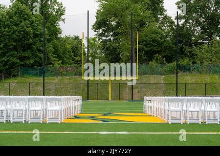 White chairs set-up in rows on a green synthetic turf athletic field ...
